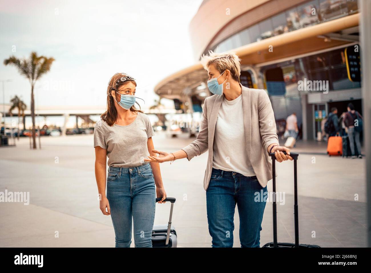 Traveling women in protective masks talking when leaving the airport at ...