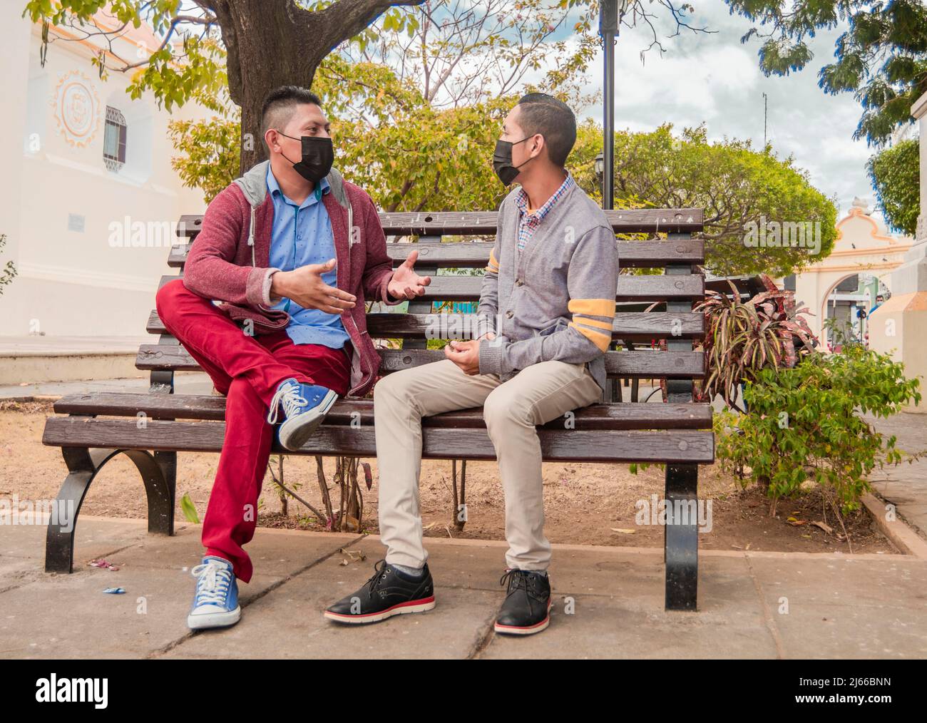 Two men with masks talking on a bench, men with social distance talking ...