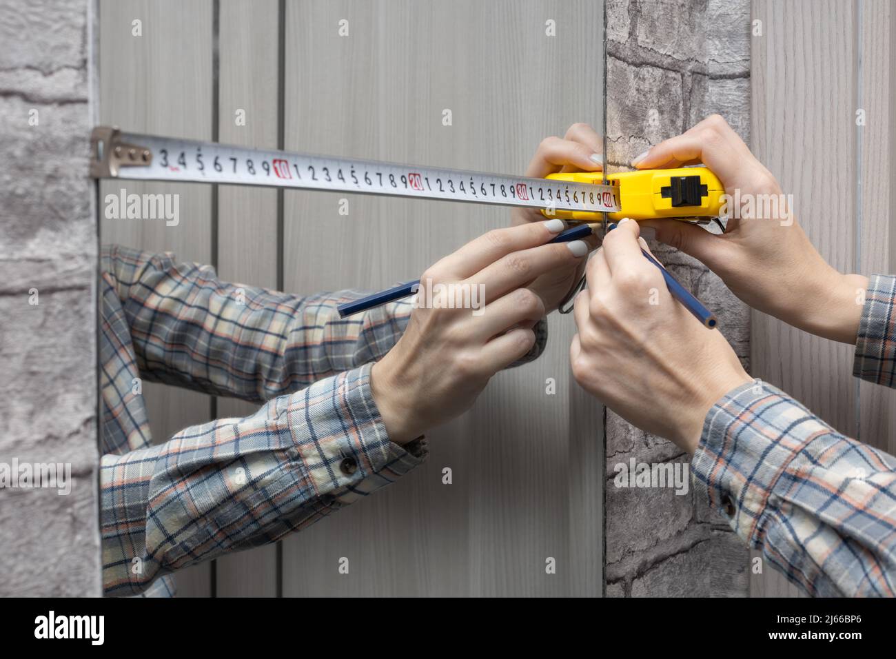 a woman measures a mirror fixed on the wall with a tape measure. High ...