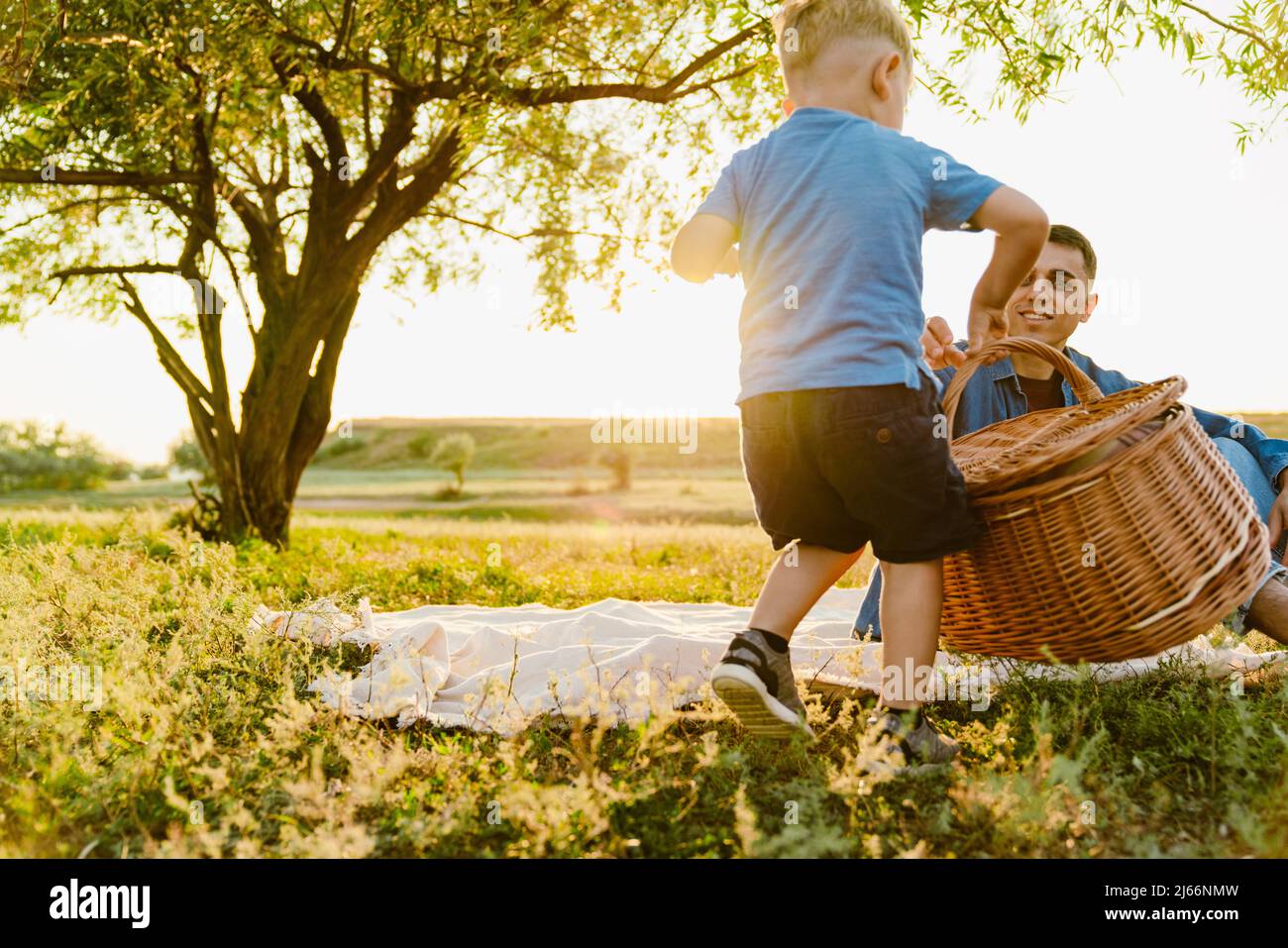 Young white father having picnic with his son by tree on summer field ...