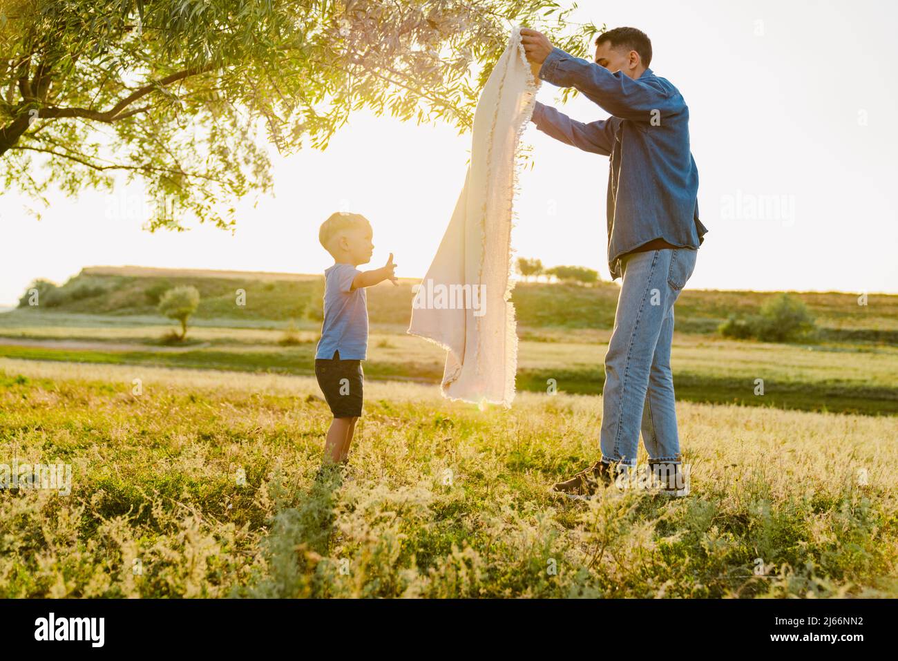 Young white father having picnic with his son by tree on summer field ...