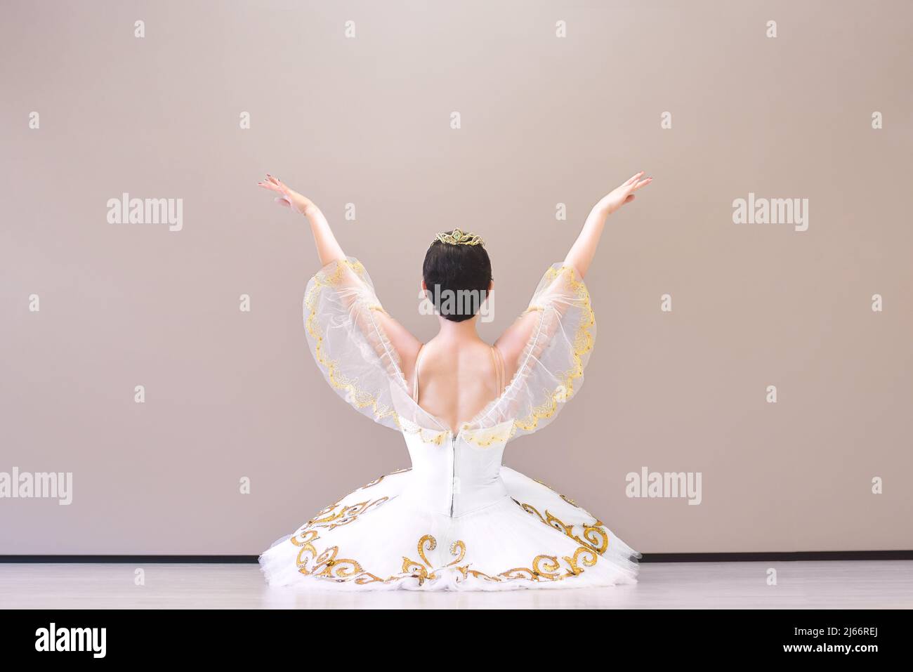 Portrait from back view of a charming ballerina is sitting on the floor ...