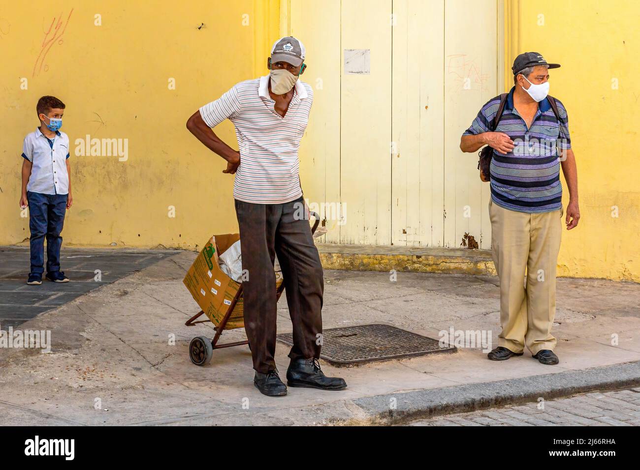 A Cuban man with a small cart is seen on a city corner. Other people ...