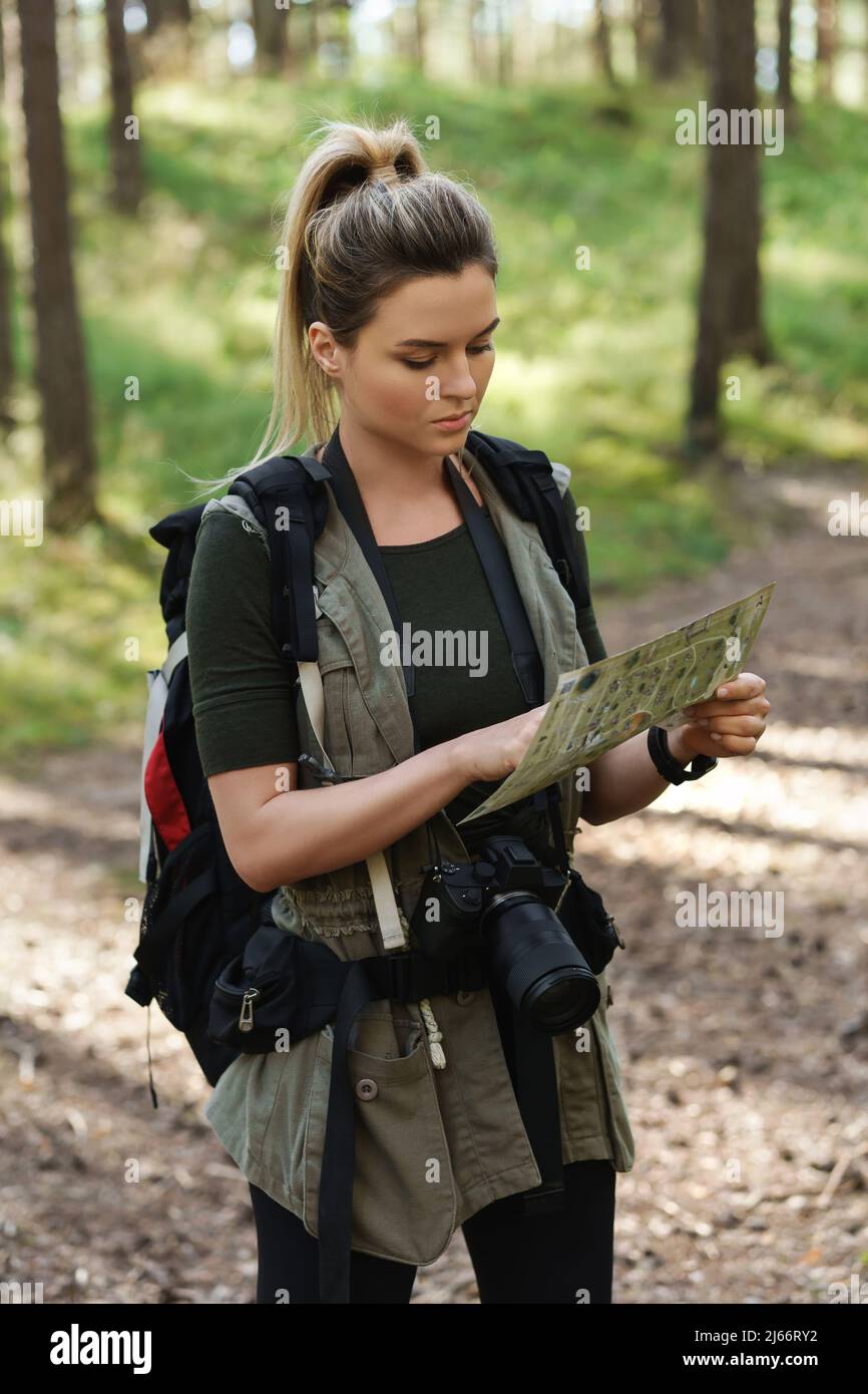 Female hiker with big backpack using map for orienteering in the forest ...