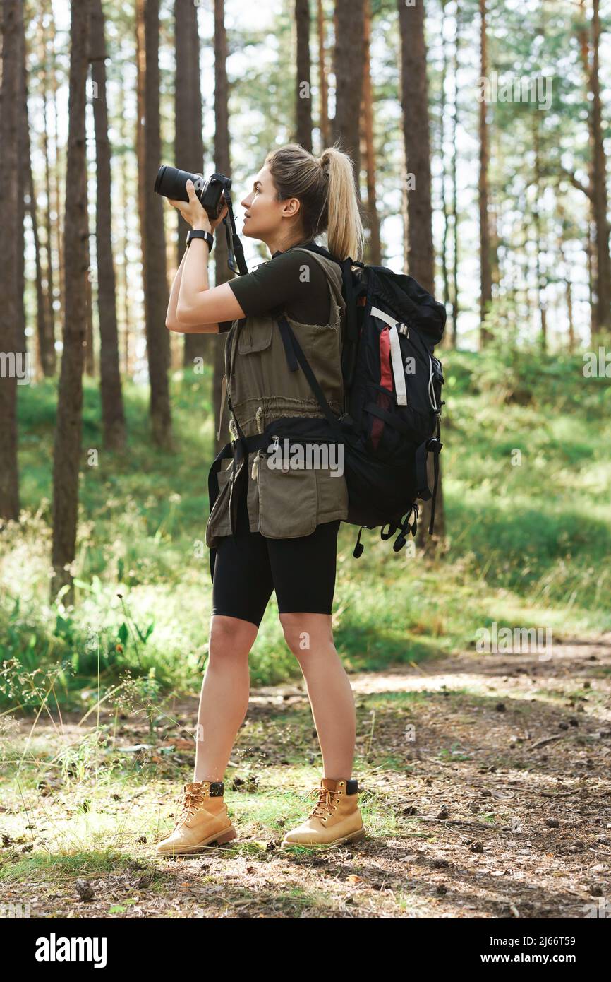 Hiker taking photos using modern mirrorless camera in green forest ...