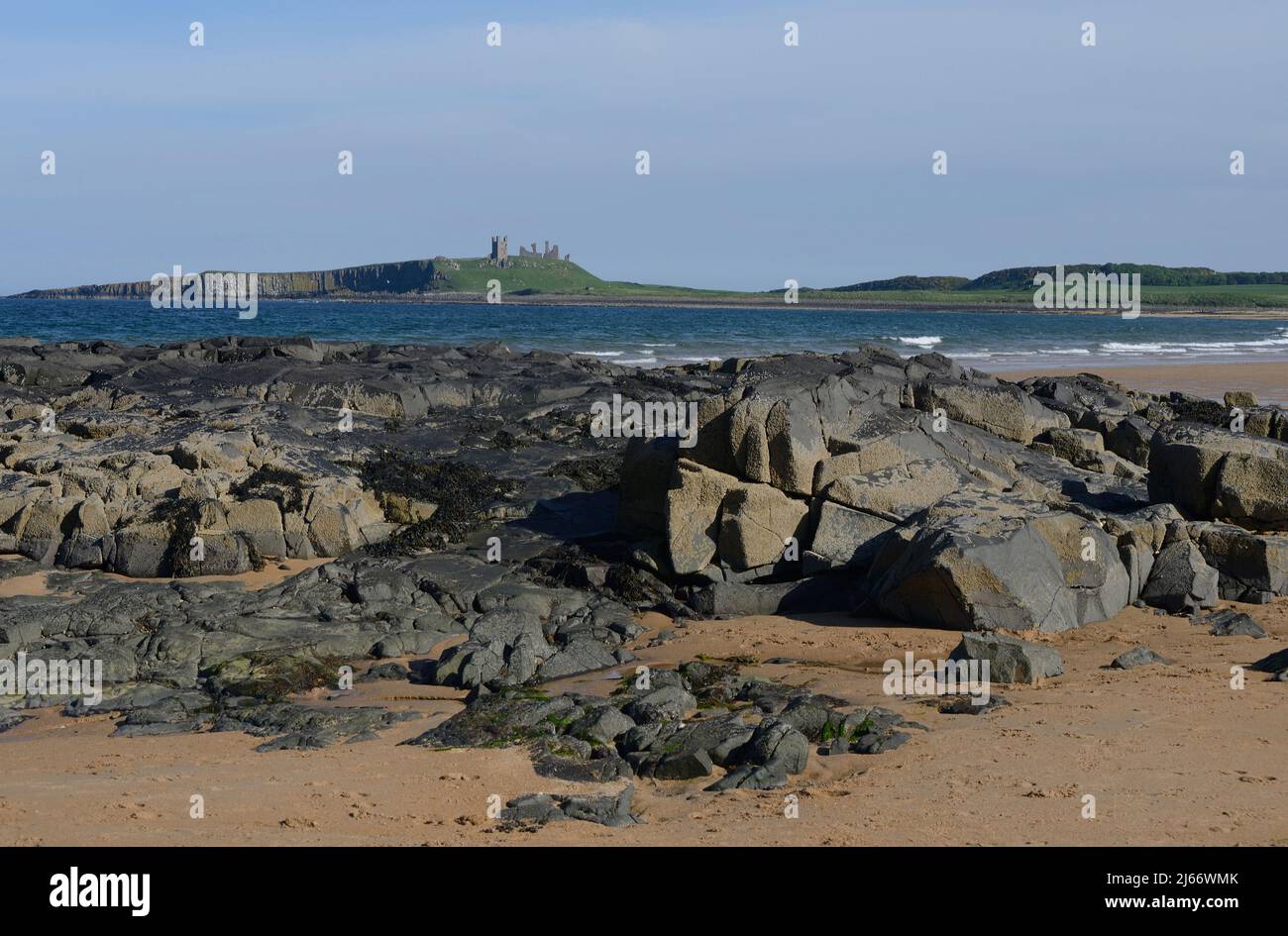A distant Dunstanburgh Castle as seen from among the basalt rocks of ...