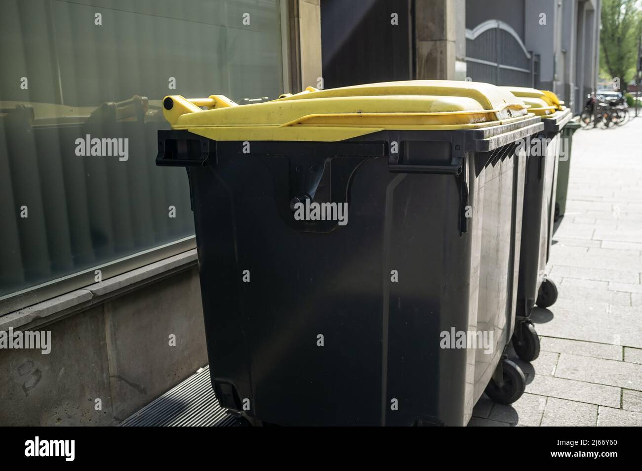 Plastic garbage containers stand near the buildings showcase, on a city ...