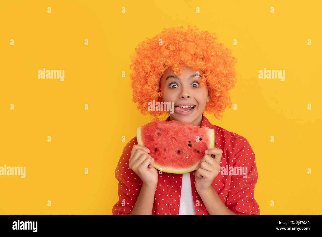 happy hungry child in fancy orange hair wig hold fresh ripe water melon ...