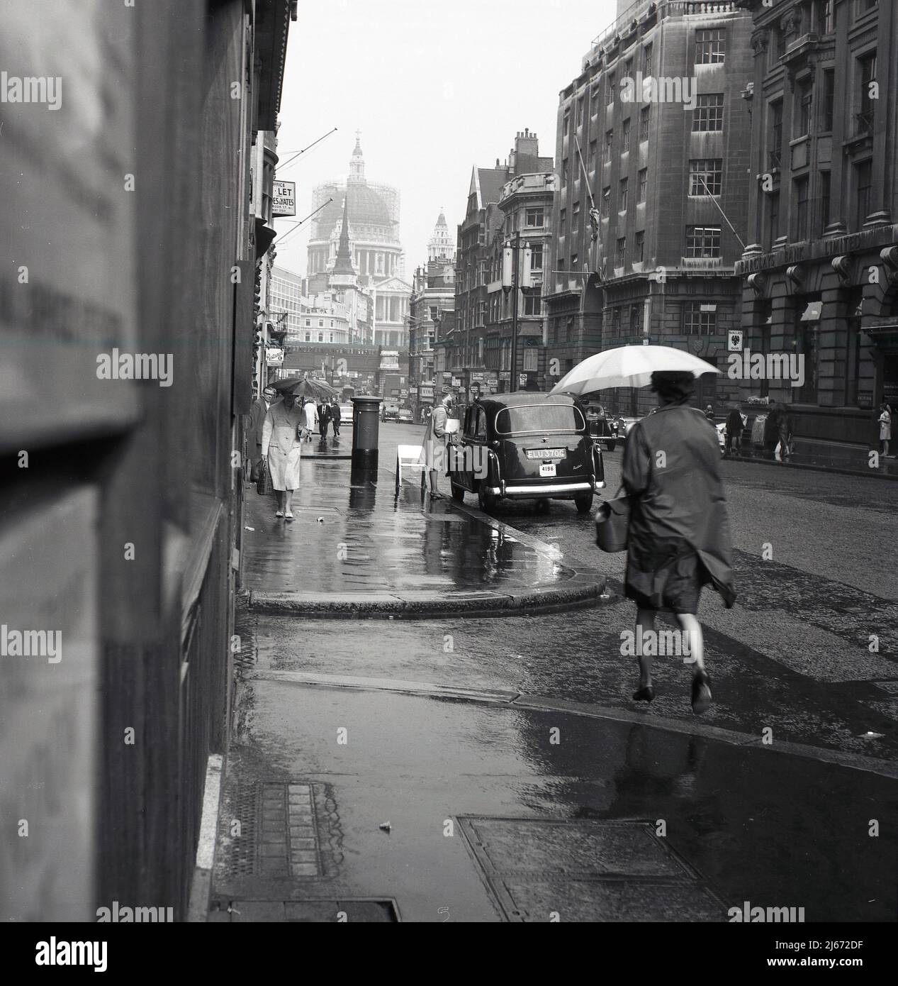 1960s, historical, wet London, a lady in a raincoat with an umbrella ...