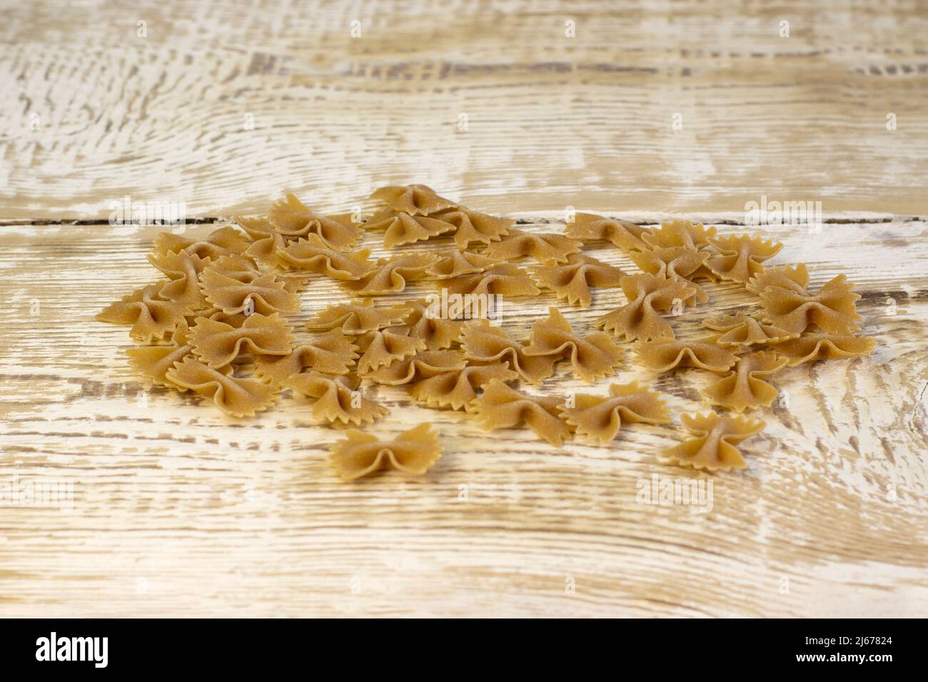 Whole grain dark pasta bows on brown plate on a rough wooden light ...