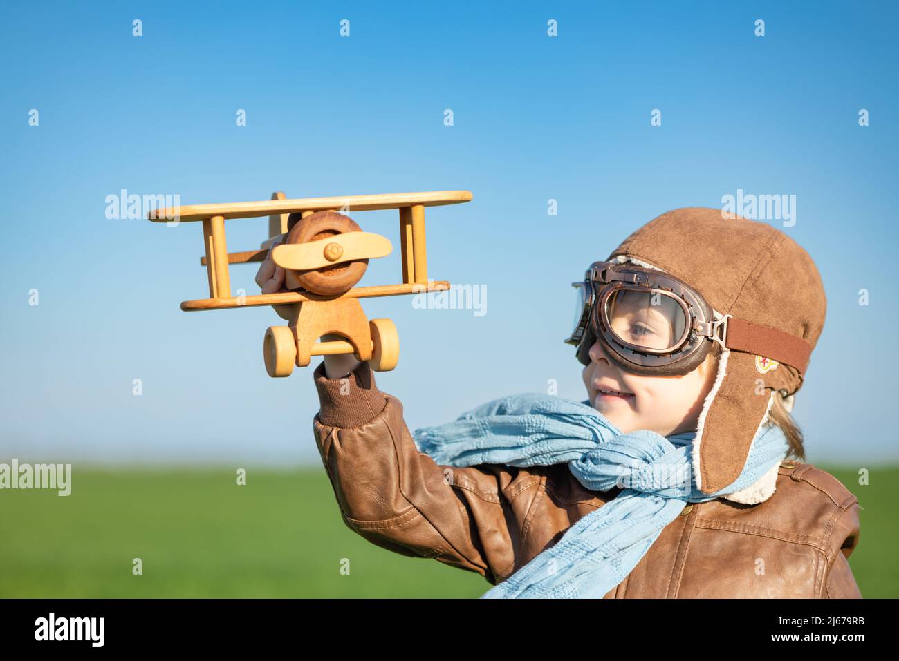 Happy child playing with wooden airplane outdoor in spring green field ...