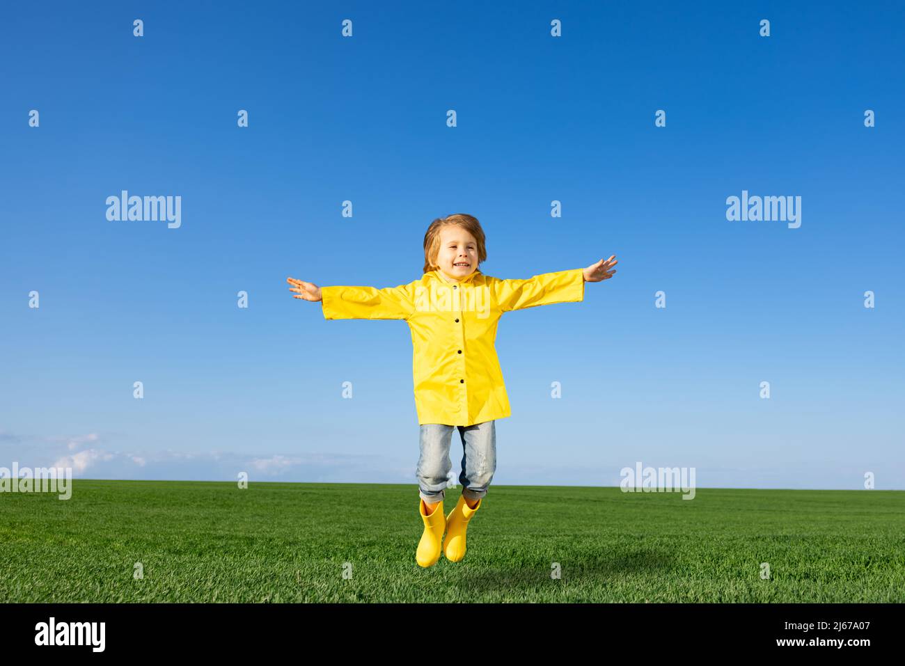 Happy child jumping in green spring field. Kid having fun against blue ...