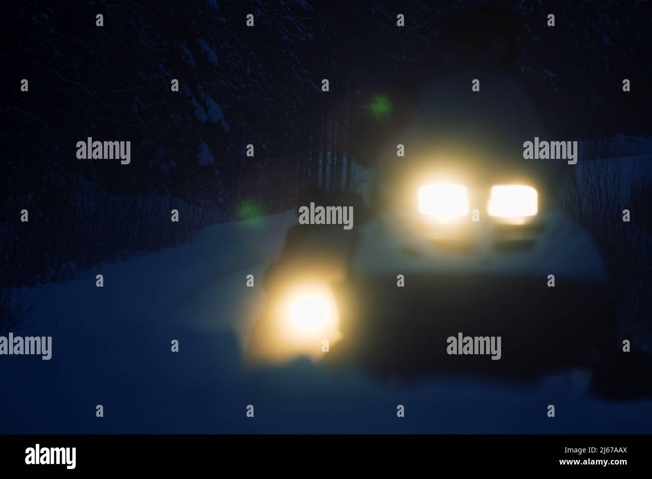 Two snowmobiles rides on a snowy forest road at night with its ...