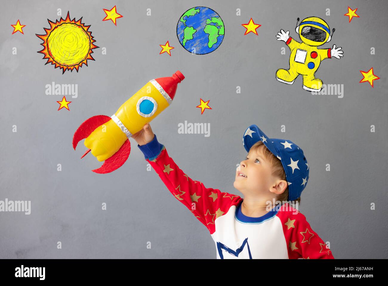 Happy child playing with toy rocket against concrete wall background ...