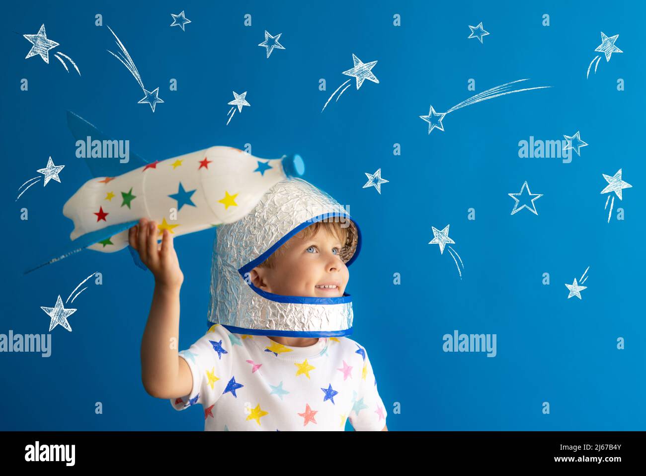 Happy child playing with toy rocket against blue background. Kid ...