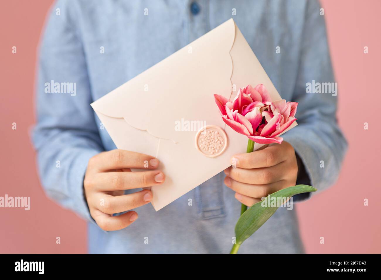 Anonymous child holding pink envelope with gift certificate and tulip ...
