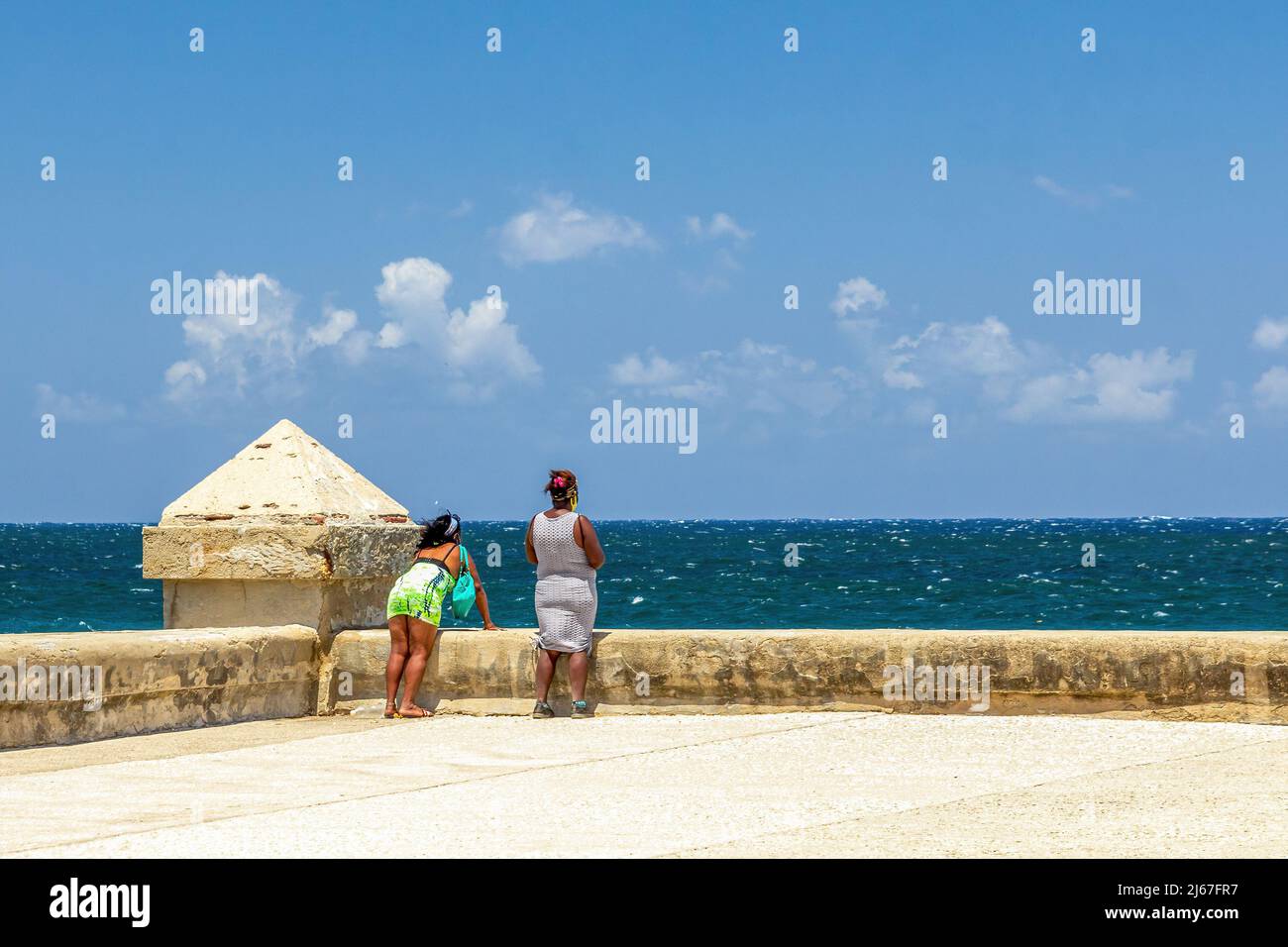 Two Cuban Afro-Caribbean women relax in the El Malecon seawall. It is a ...