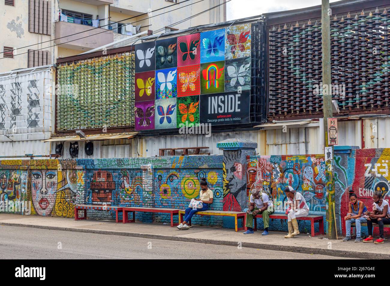 Cuban people are sitting in benches on a sidewalk in the capital city ...