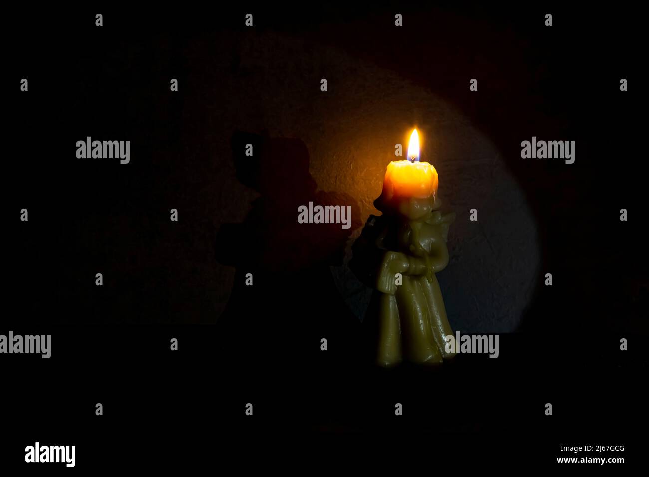 Wax candle in the shape of an angel. Shadow of an angel on a dark wall ...