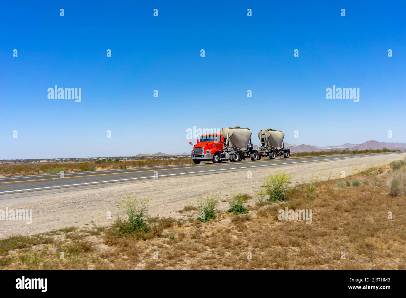 Red semi-truck pulling a double dry bulk trailer on a rural highway in ...