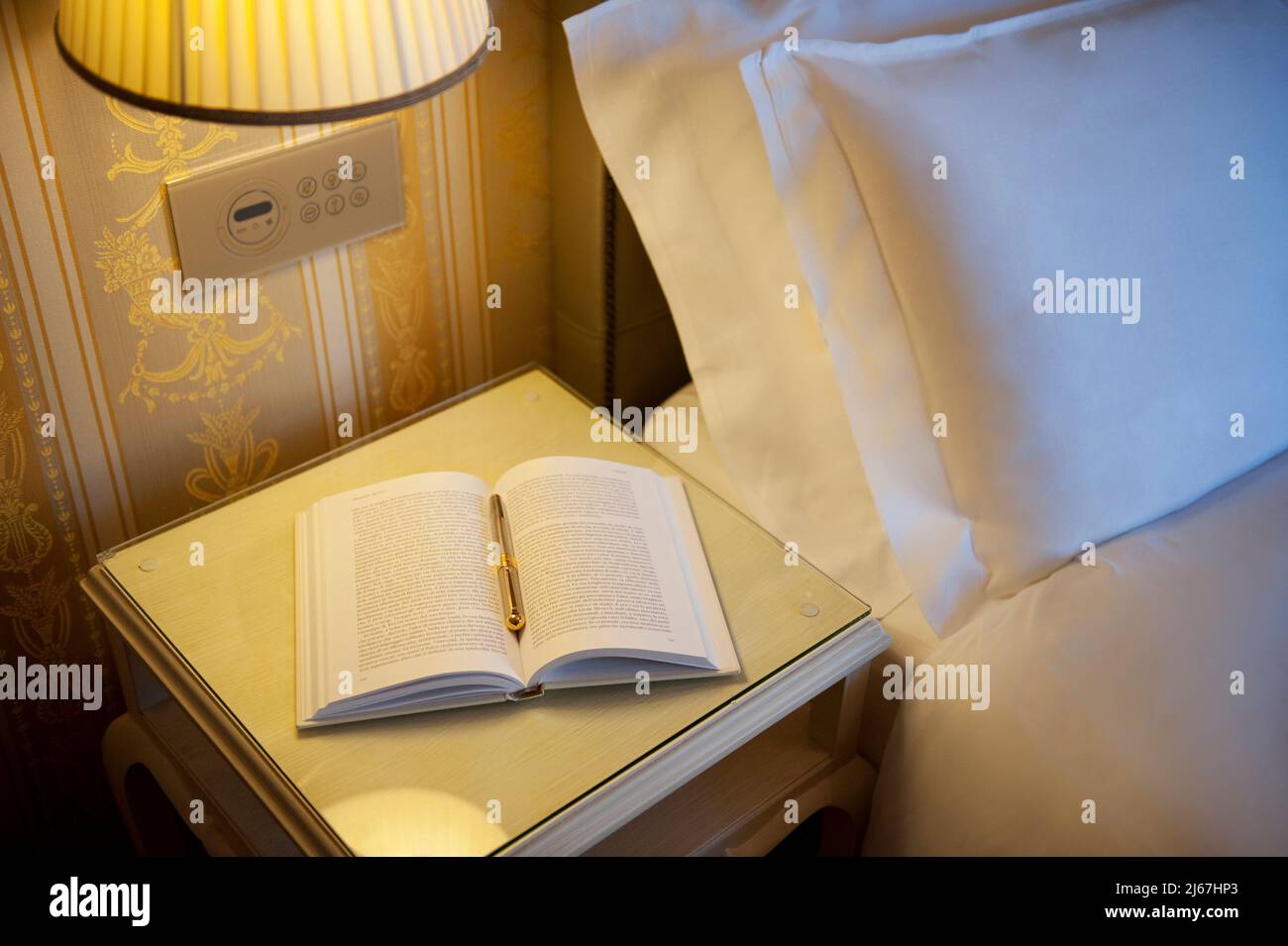 Luxury hotel room with a book and a golden pen on the side bed table ...