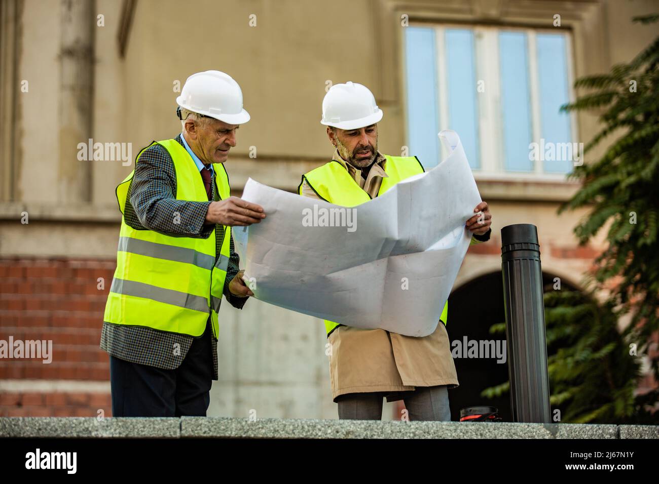 Two construction workers are looking at the plans on the paper while ...