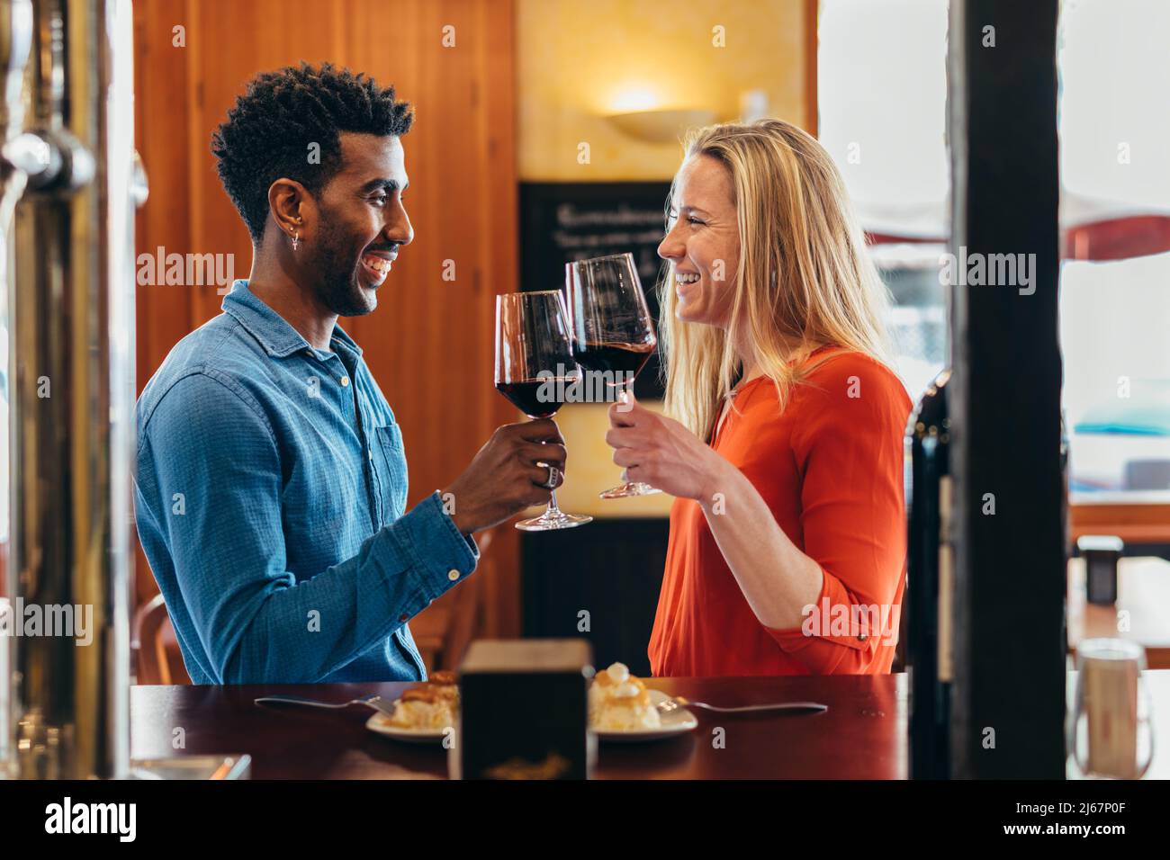 multiethnic couple celebrating with a red wine toast at the bar of a ...