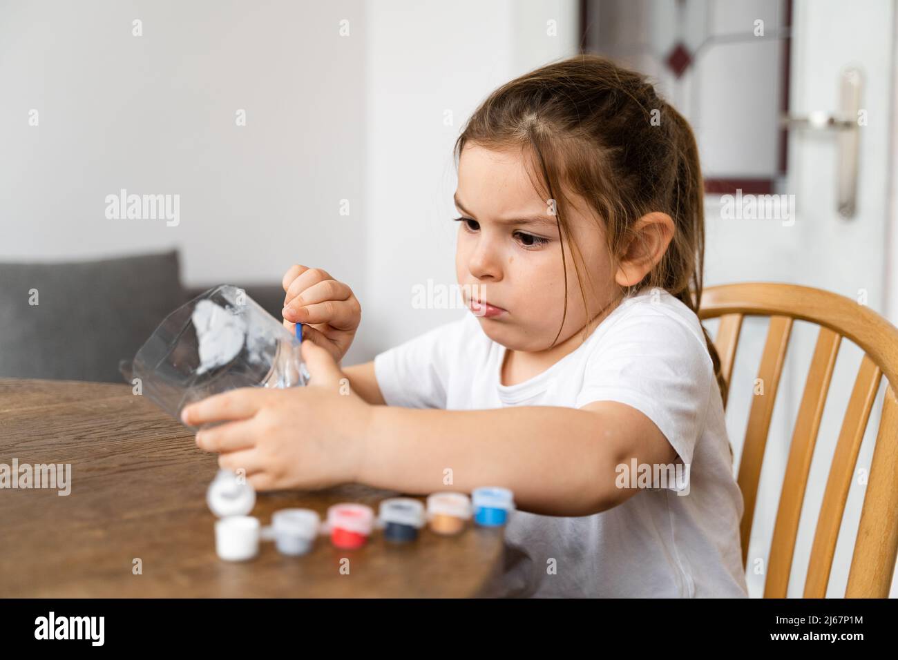 Caucasian preschool girl doing crafts with plastic bottle and paints ...