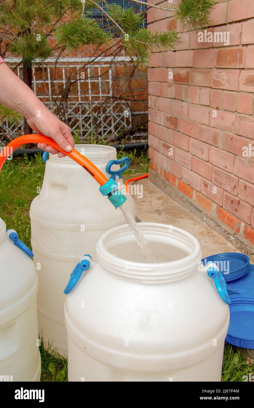 A woman's hand fills a plastic barrel with water from a hose. The ...