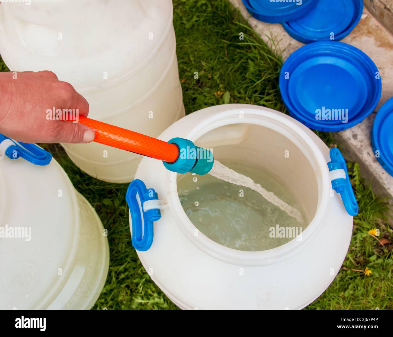 A woman's hand fills a plastic barrel with water from a hose. The ...