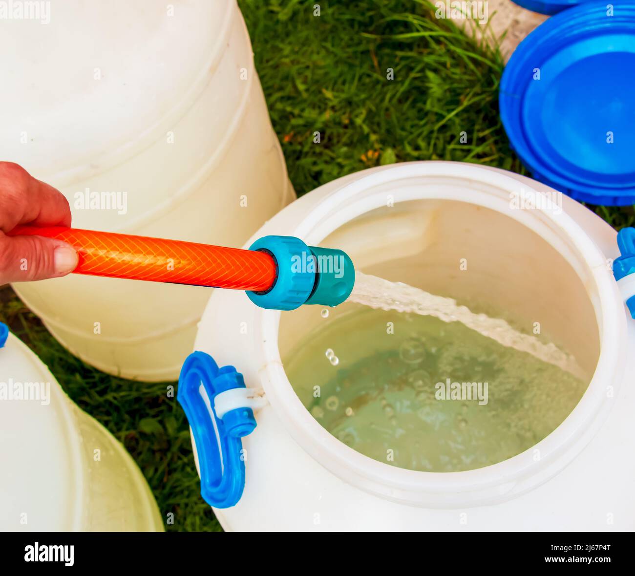 A woman's hand fills a plastic barrel with water from a hose. The ...