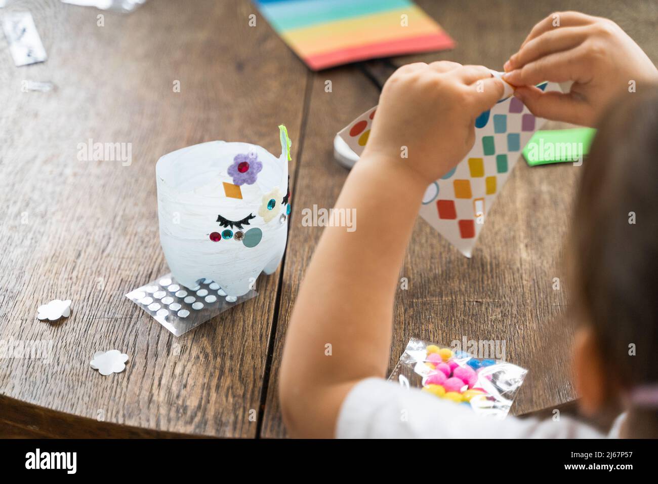Caucasian preschool girl doing crafts with plastic bottle and paints ...