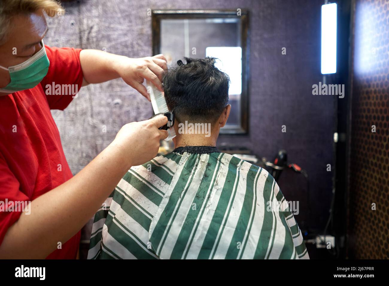 Back of a client sitting while having his hair cut in a barber shop ...