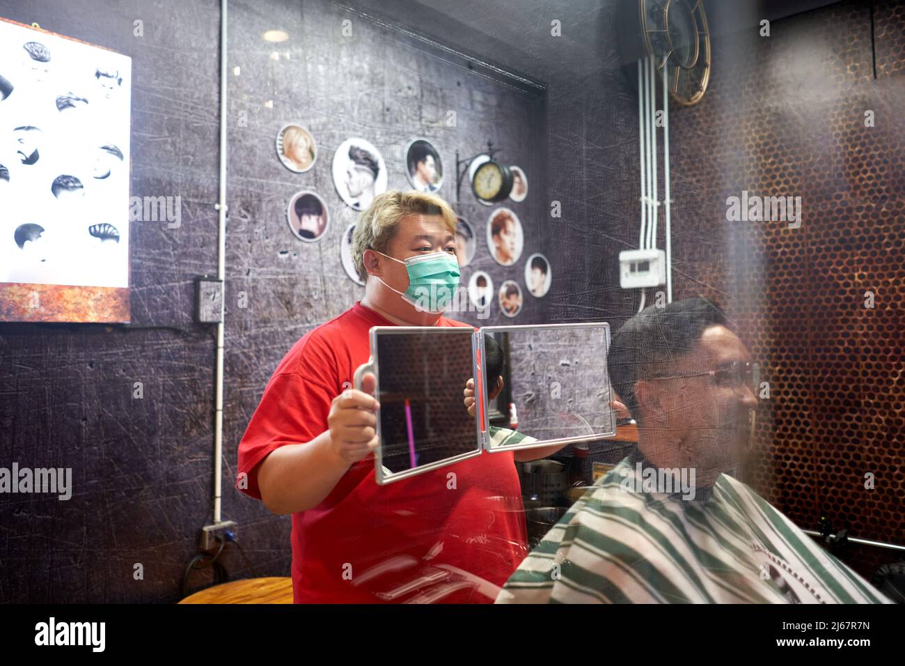 Obese barber holding a mirror to show the haircut to a client in a ...