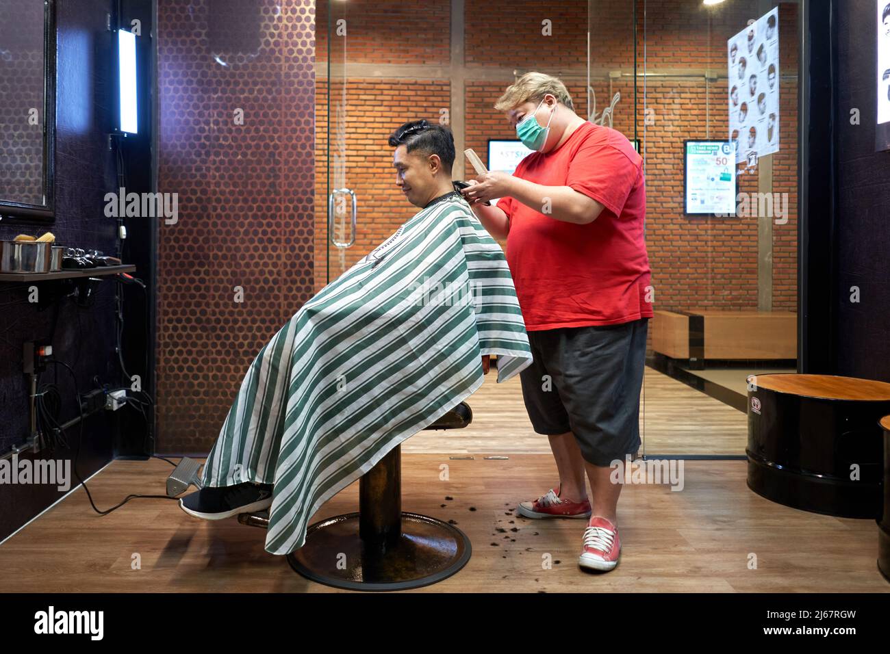 Obese barber standing cutting the hair of a gay asian client in a ...