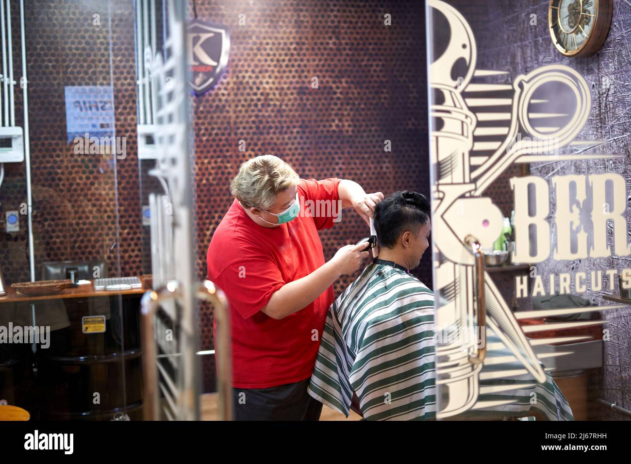 Fat barber standing cutting the hair of an asian client in a barber ...