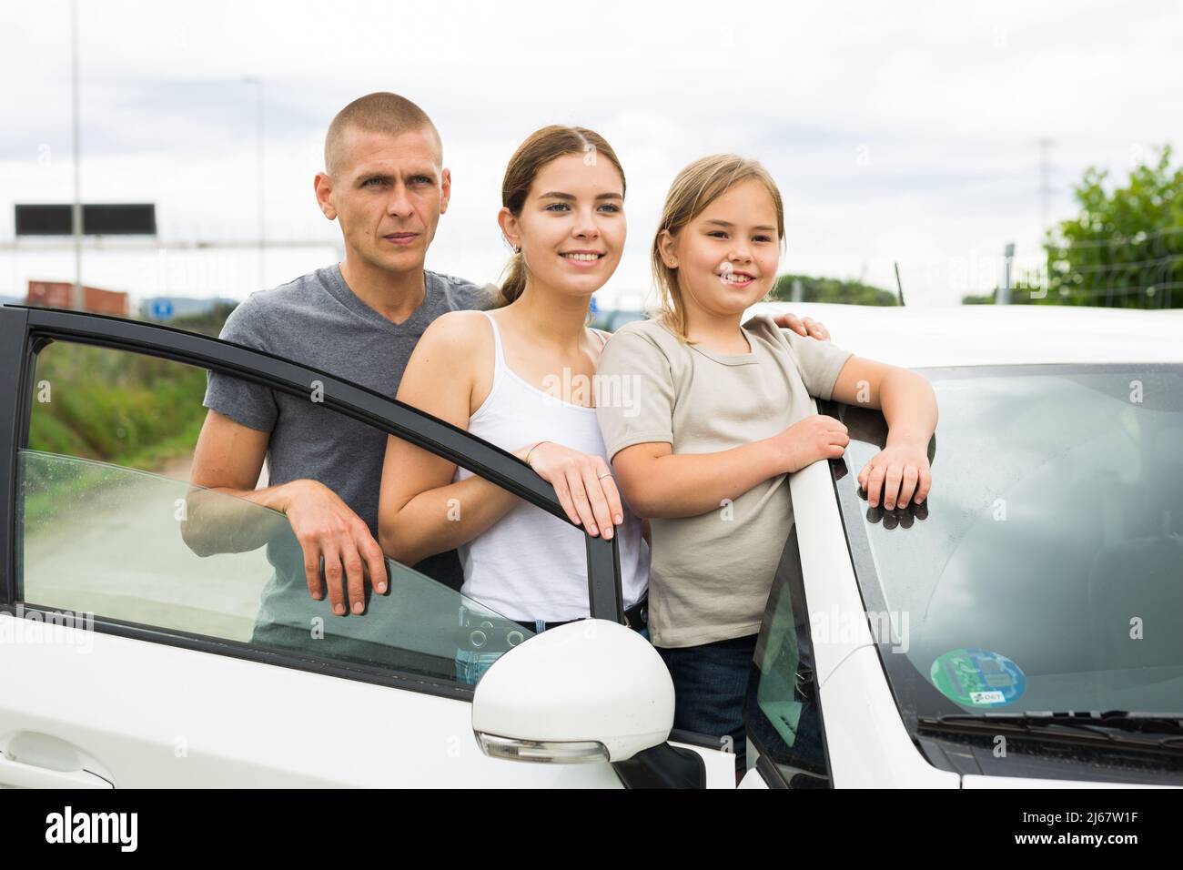 Positive family standing near an open car Stock Photo - Alamy