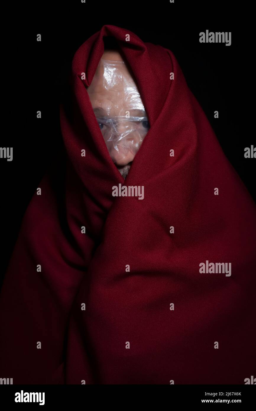 Man covered in red cloth with plastic on his face against black ...