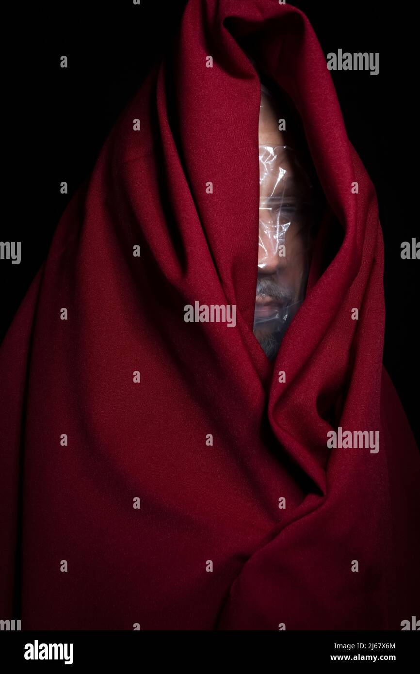 Man covered in red cloth with plastic on his face against black ...