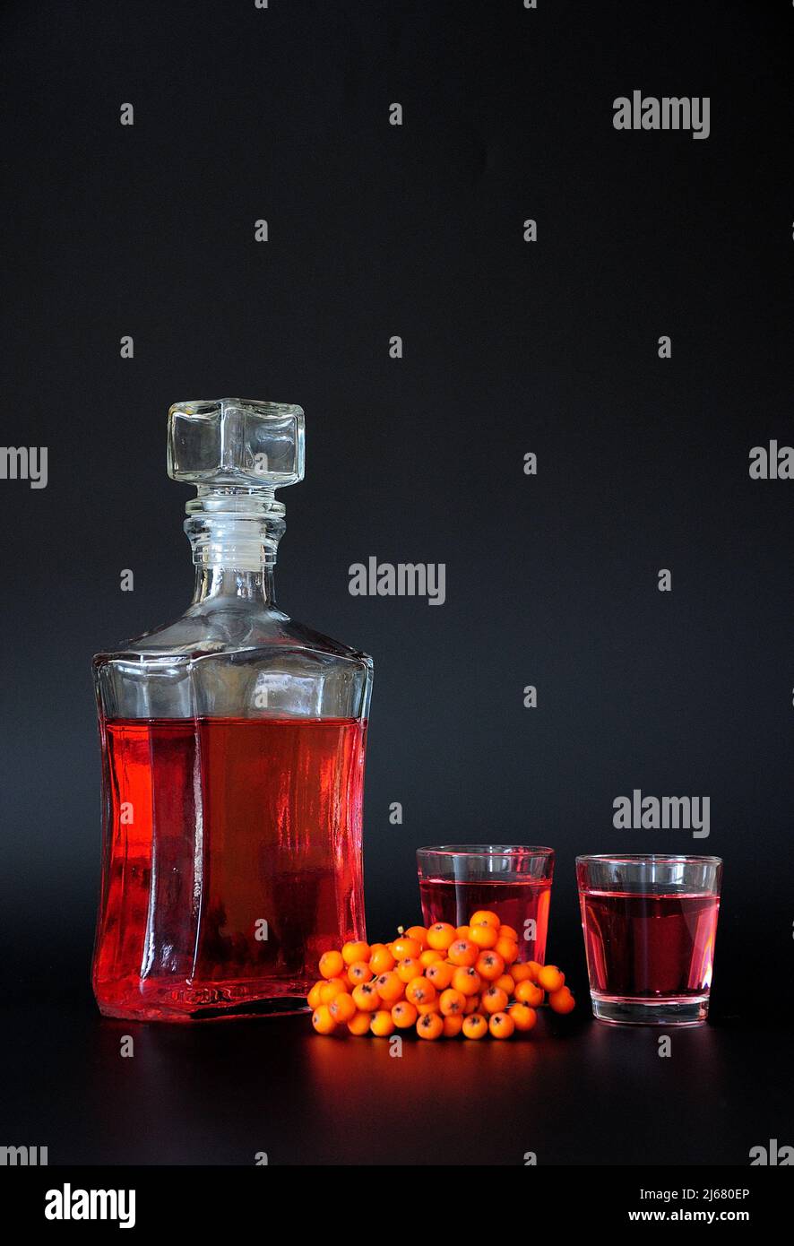 Rowan liqueur, homemade alcohol and a sprig of ripe berries on a black ...