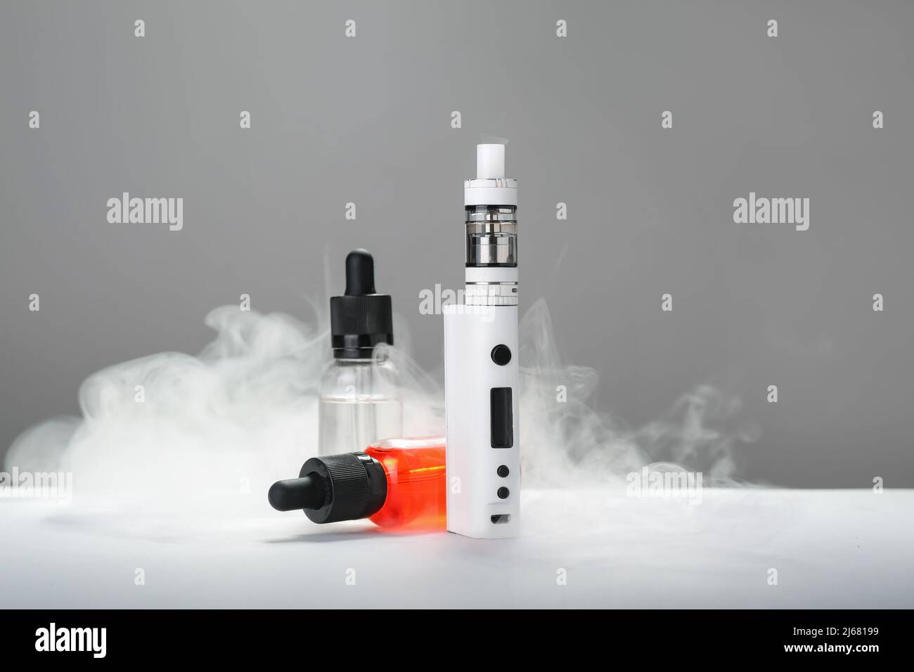 Modern vape mod and oils with smoke on grey background Stock Photo - Alamy