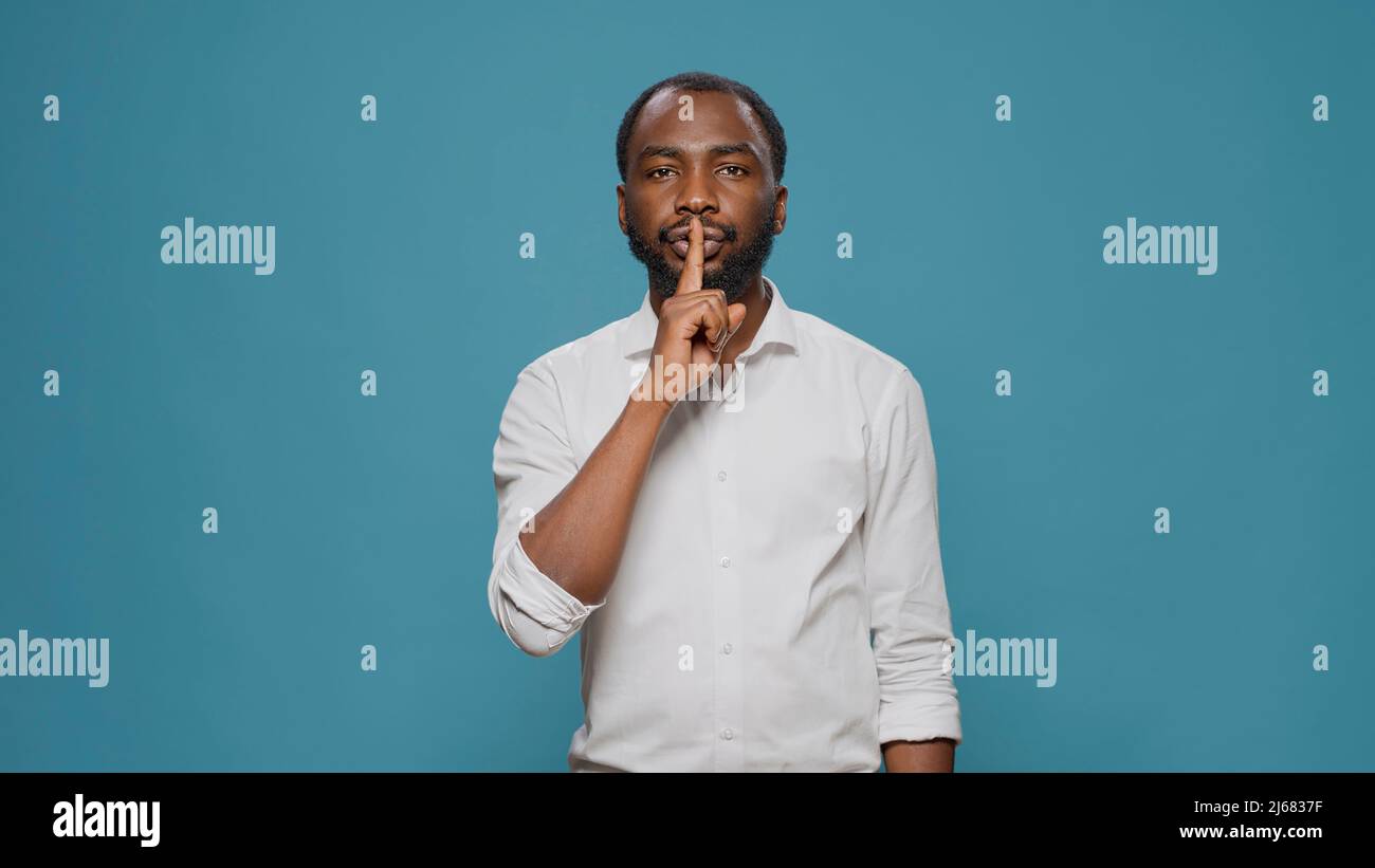 Portrait of male model showing silence sign in front of camera, putting ...