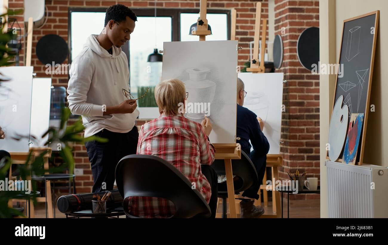 Male teacher giving advice to elder woman in drawing class, learning ...
