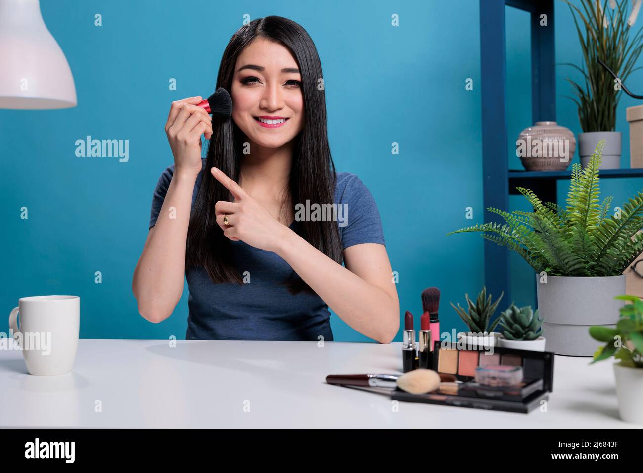 Asian content creator using brush while doing makeup tutorial at camera ...
