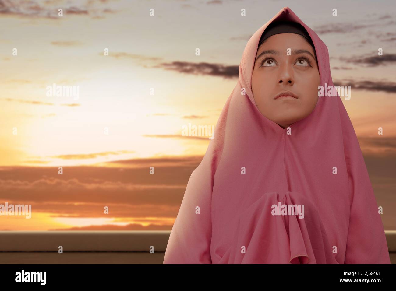 Asian Muslim woman in a veil standing while raised hands and praying in ...