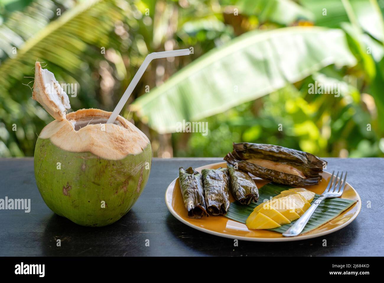 Thai style dessert, yellow mango with banana sticky rice in palm leaves ...