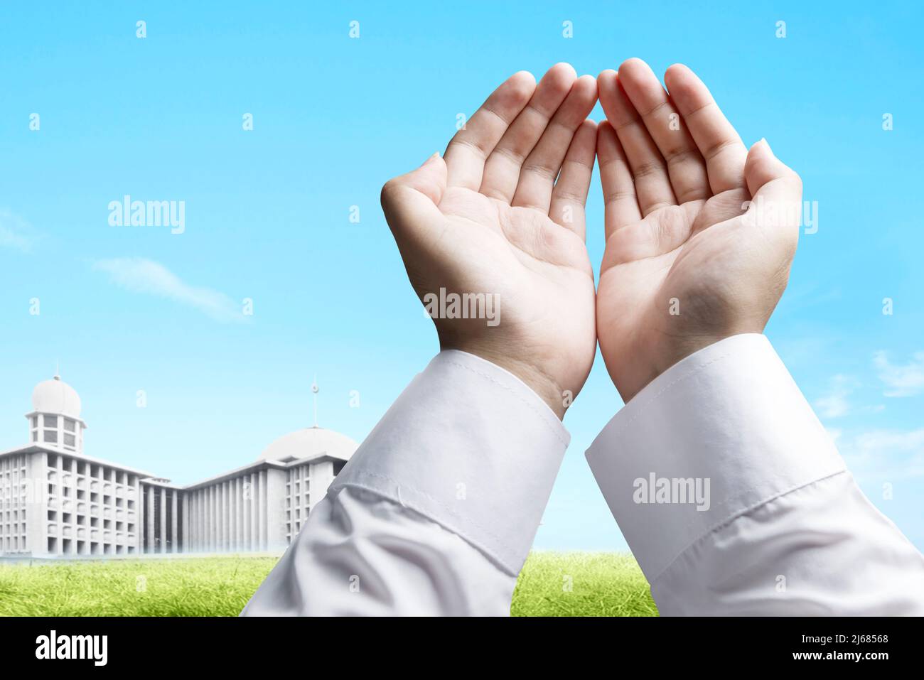 Muslim man standing while raised hands and praying with mosque view ...