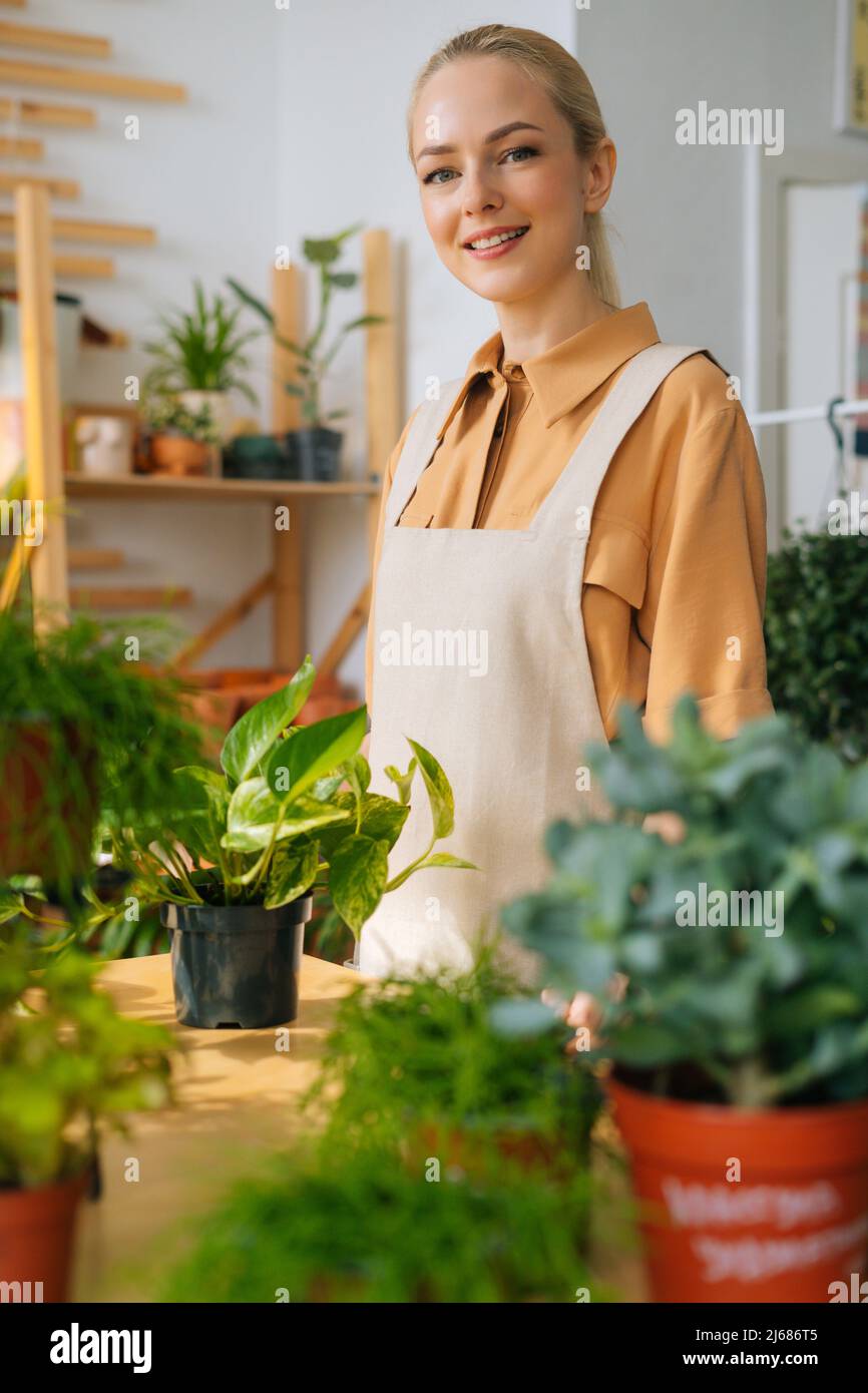 Vertical portrait of smiling young woman florist in apron standing near ...