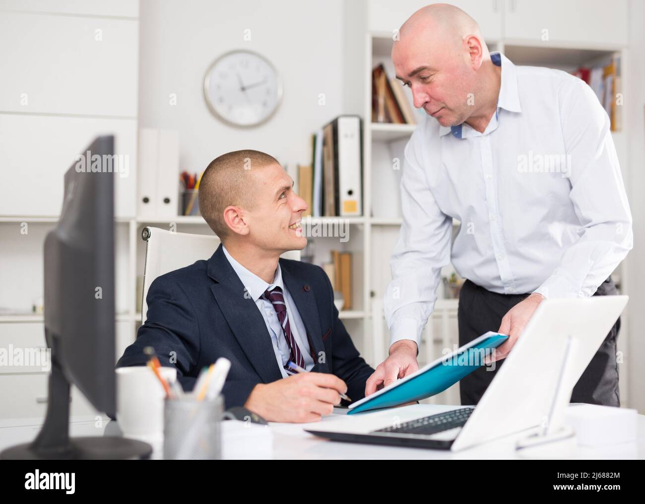 Two male employees are smiling and signing documents Stock Photo - Alamy