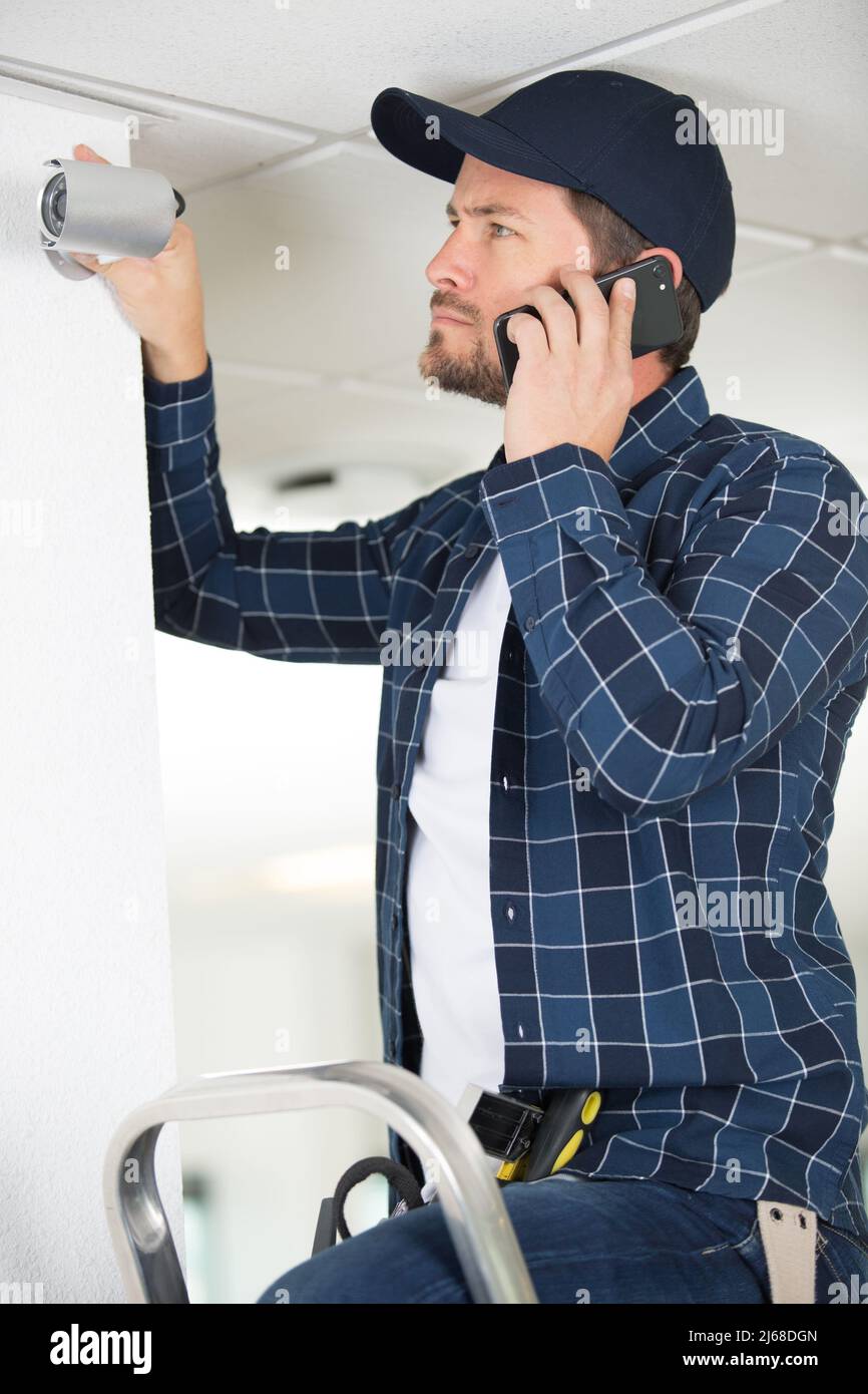 technician on the phone fixing cctv camera on wall Stock Photo - Alamy